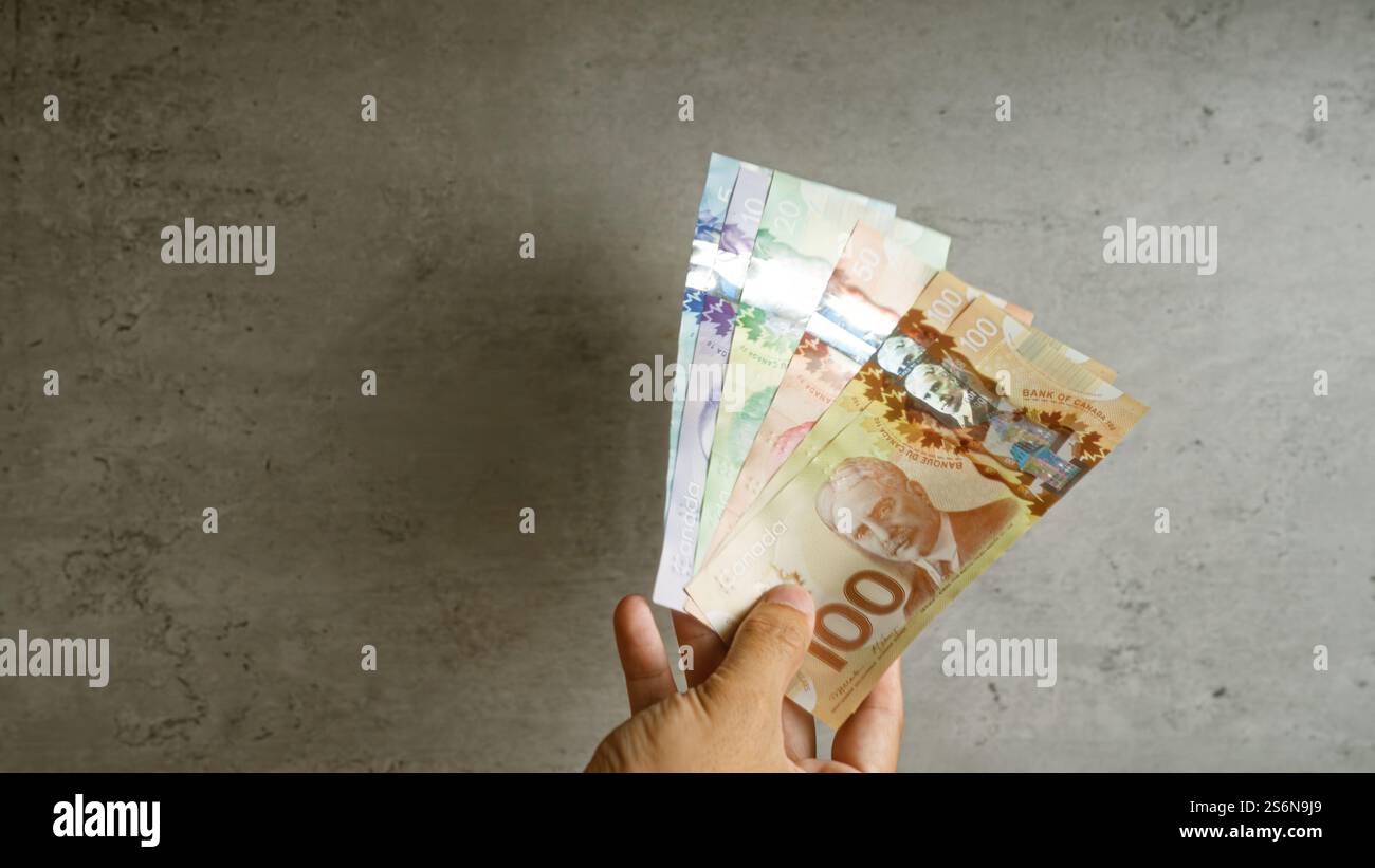 Hand holding canadian dollars against a concrete background, showcasing ...