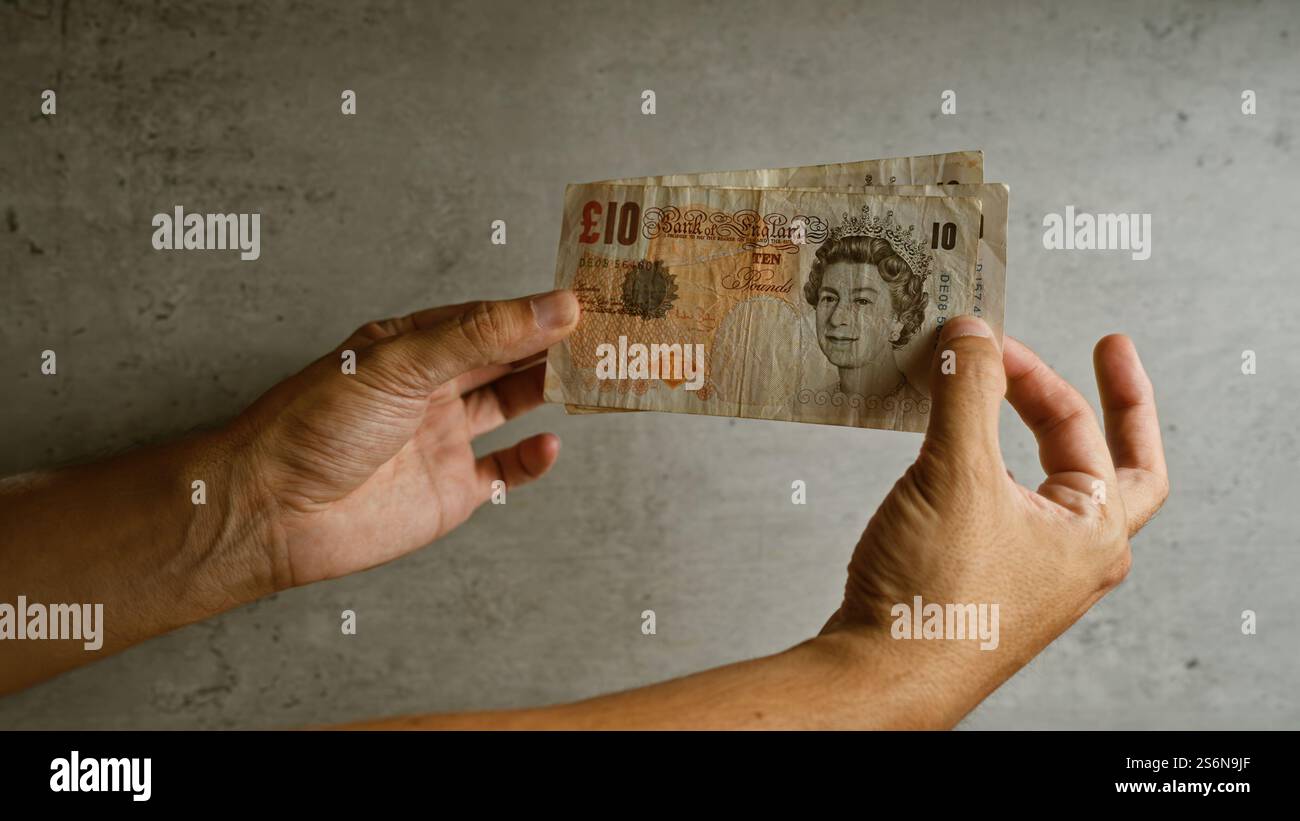 Hands holding british 10-pound banknotes with a concrete wall ...
