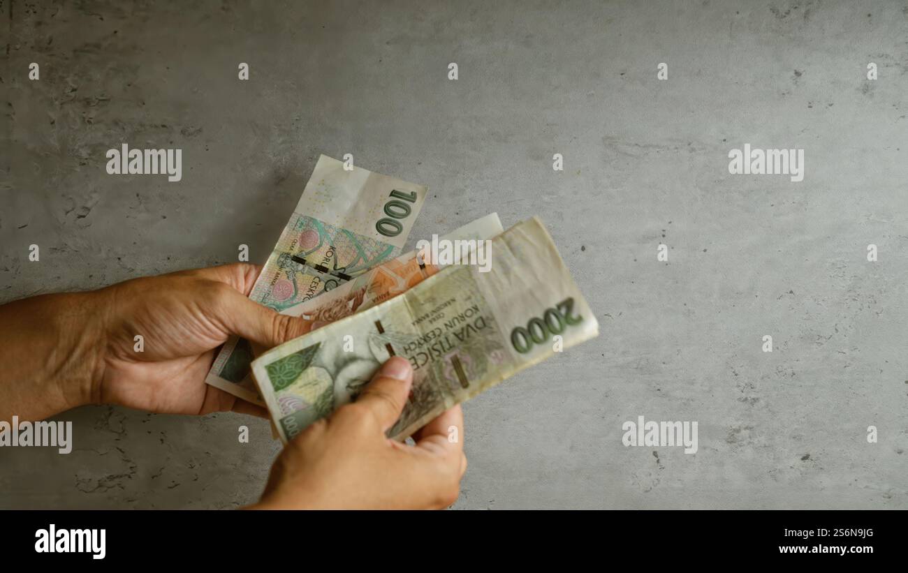 Person counting czech koruna banknotes against a concrete background ...