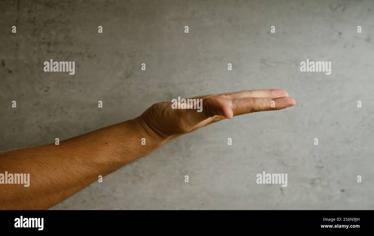 Man's hand reaching out against a textured concrete wall background, displaying an open palm and ...