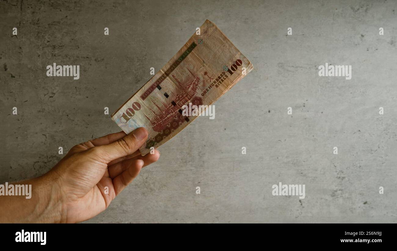Hand holding a 100 saudi riyal note against a concrete background ...