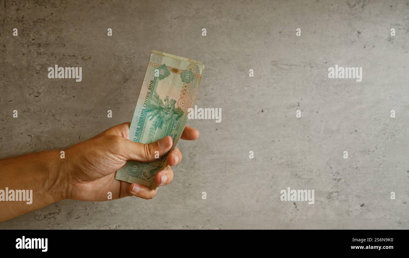 Hand holding uae dirhams against a concrete background emphasizing ...