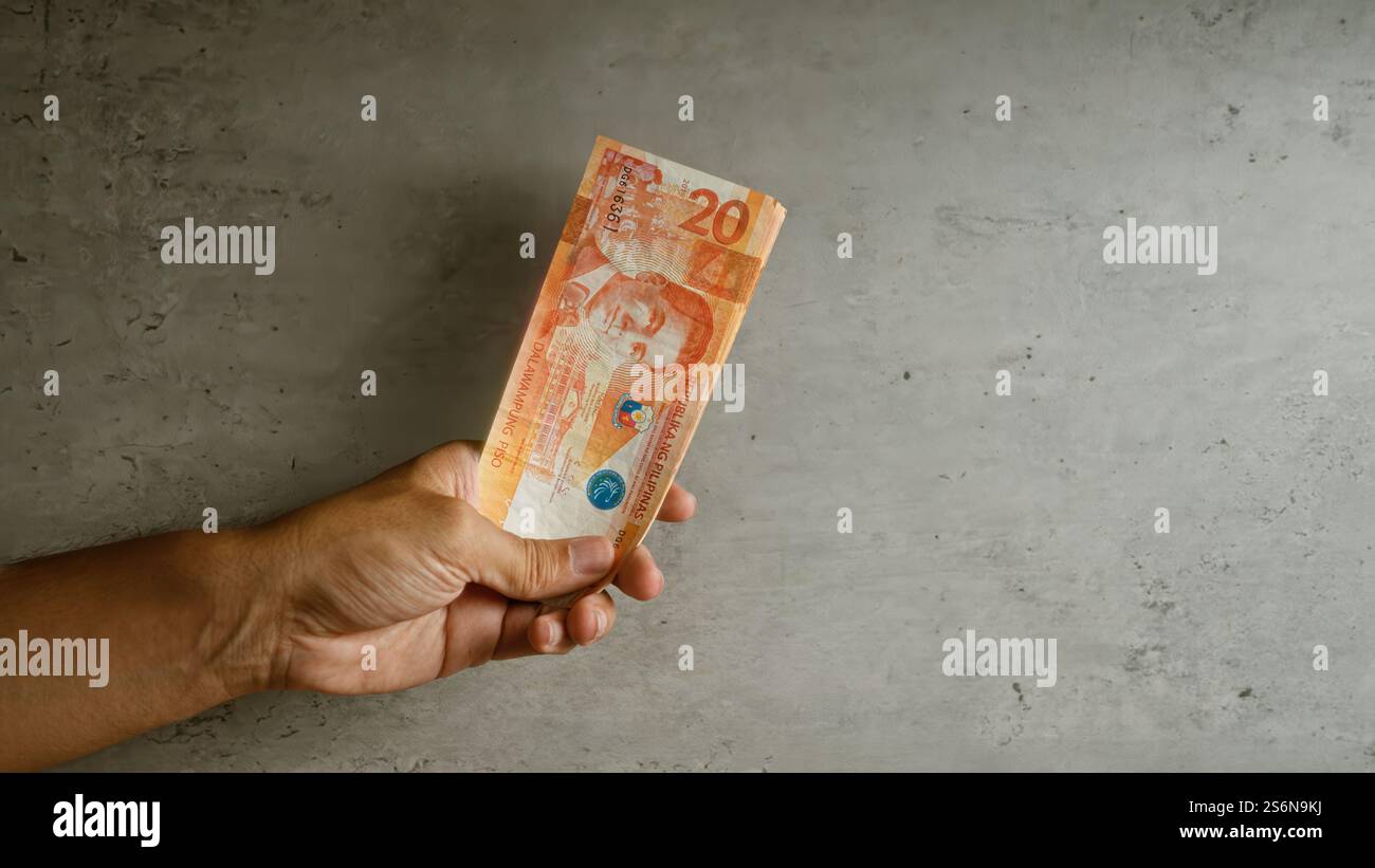 Hand holding philippine pesos against a concrete background, showcasing ...