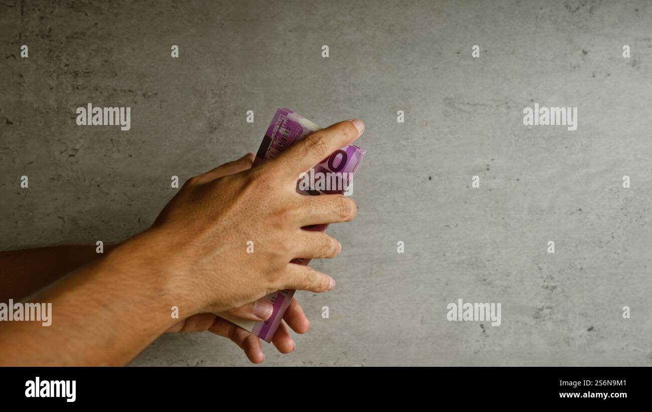 Man's hand holding filipino peso notes against a concrete background ...