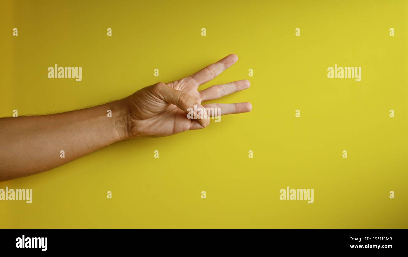 Hand showing three fingers against a vibrant yellow background with a ...