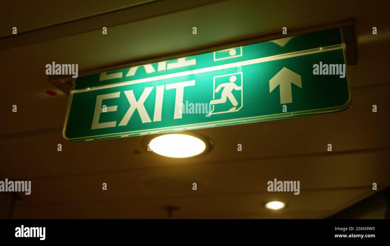 Illuminated exit sign glows green with a directional arrow indoors ...