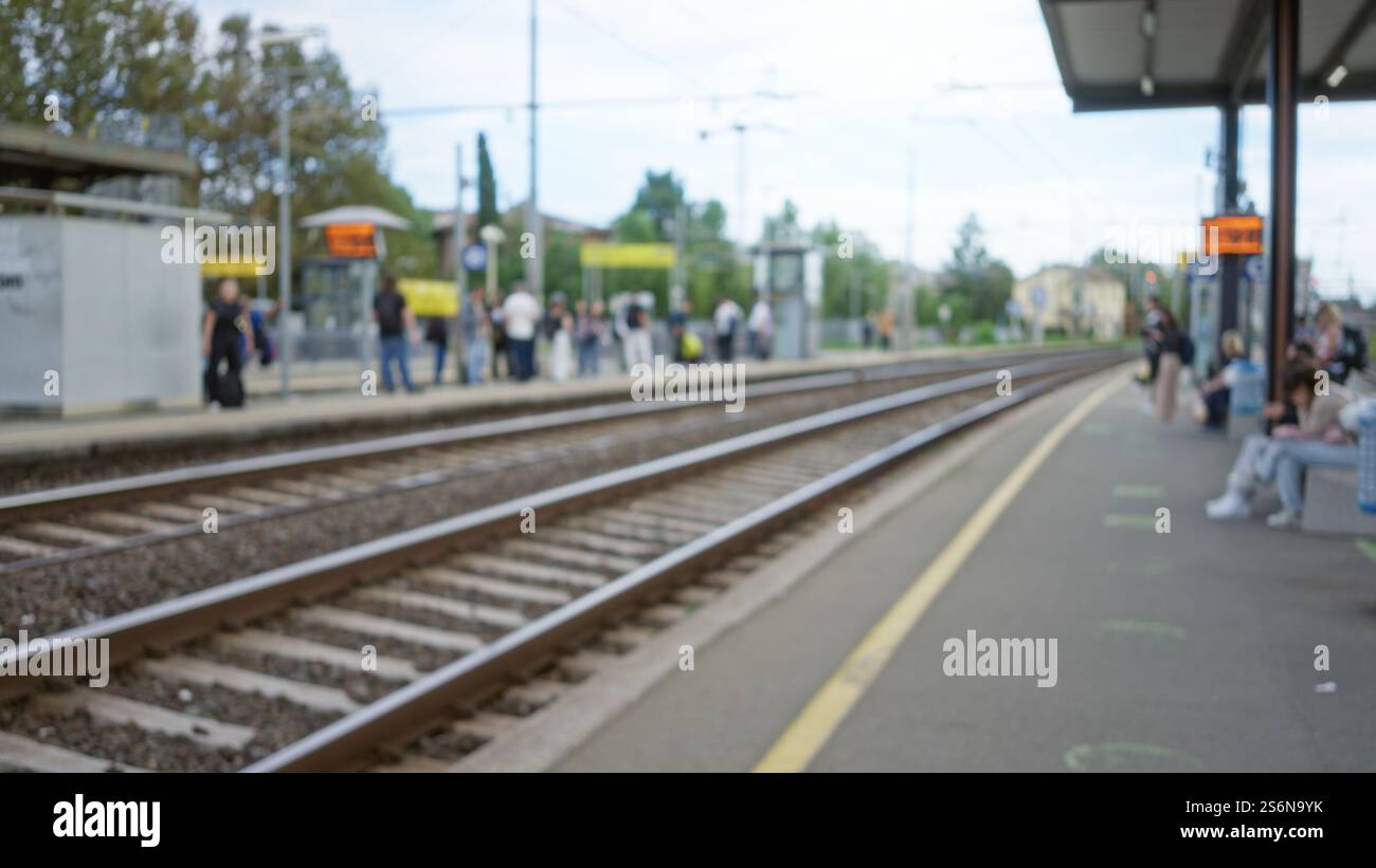 Blurry scene of people waiting at railway station with tracks and ...