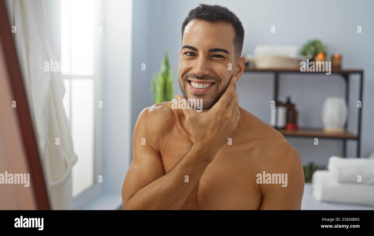 Handsome young man with a beard smiling in a spa room touching his face ...