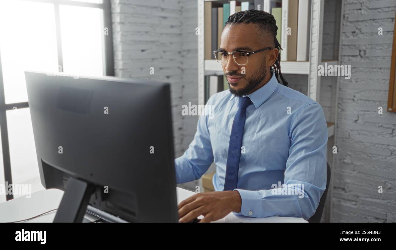 Young man with braids working at a computer in a modern office setting ...