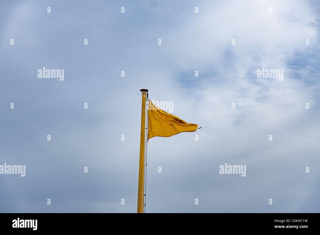 A yellow flag is flying in the sky. The sky is mostly blue with some ...