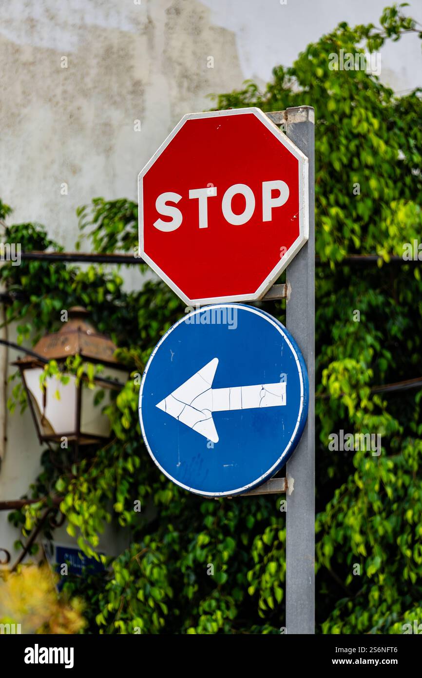 A stop sign is on a pole next to a blue arrow pointing to the left. The ...