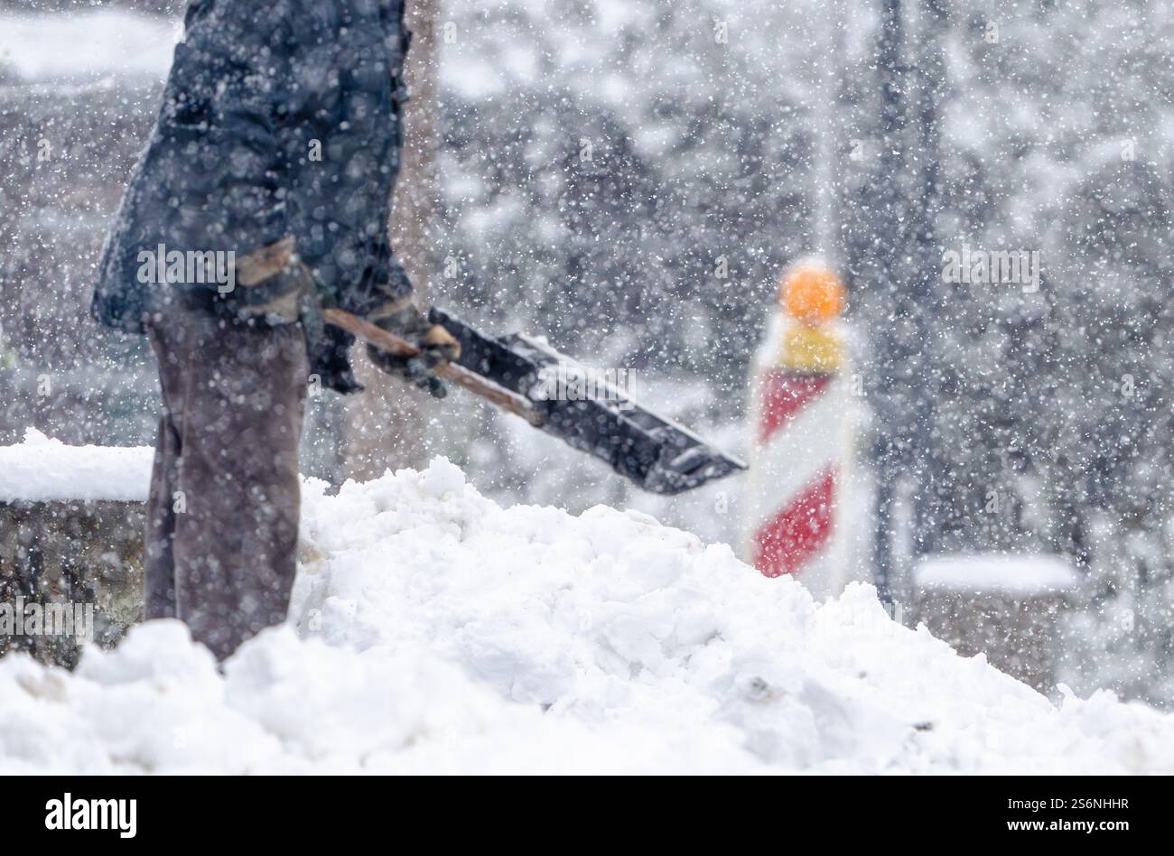 A man is shoveling snow off a sidewalk. The snow is falling and the man ...