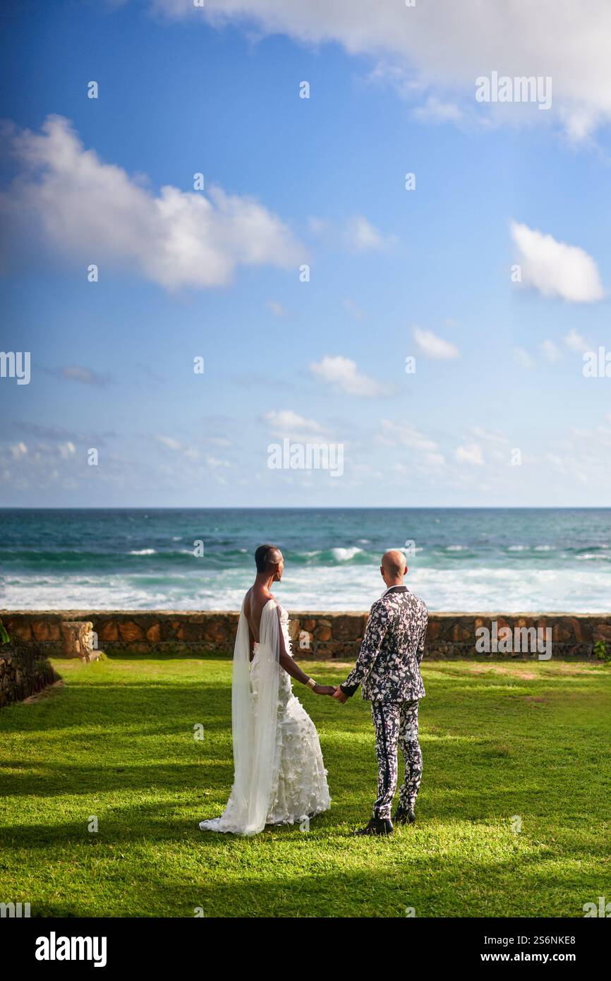 Couple at tropical villa wedding. Bride in white dress holds hands with ...