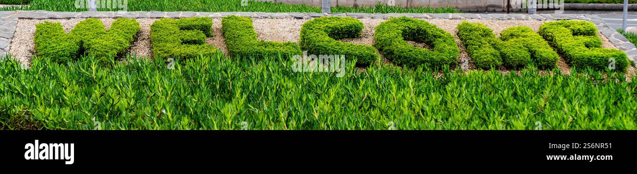 A sign with the word welcome written in grass. The sign is green and ...