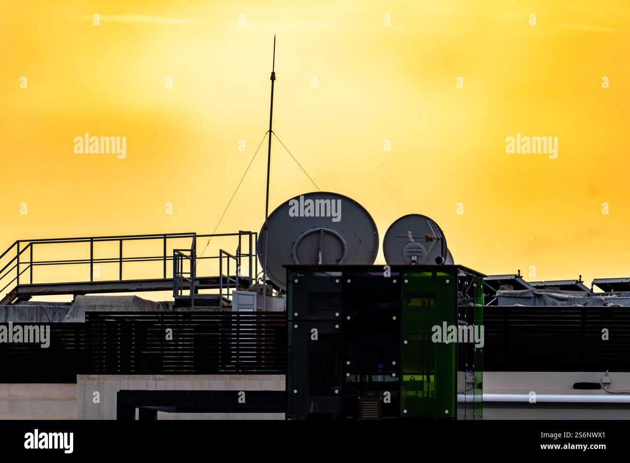 A satellite dish is on top of a building. The sky is orange and the sun ...