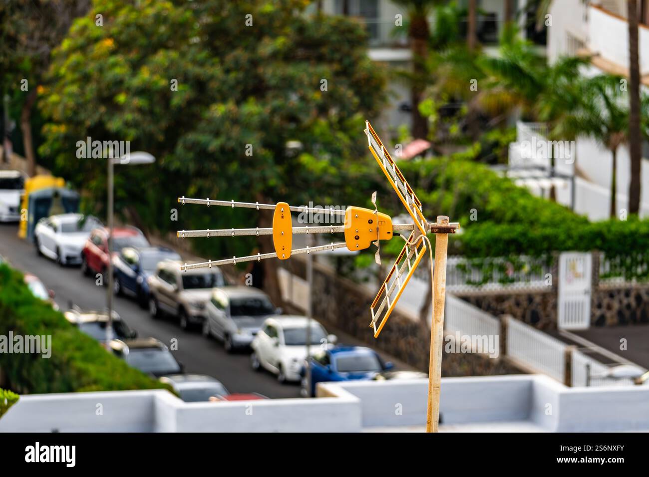 A yellow antenna is on a pole in front of a row of cars. The antenna is ...