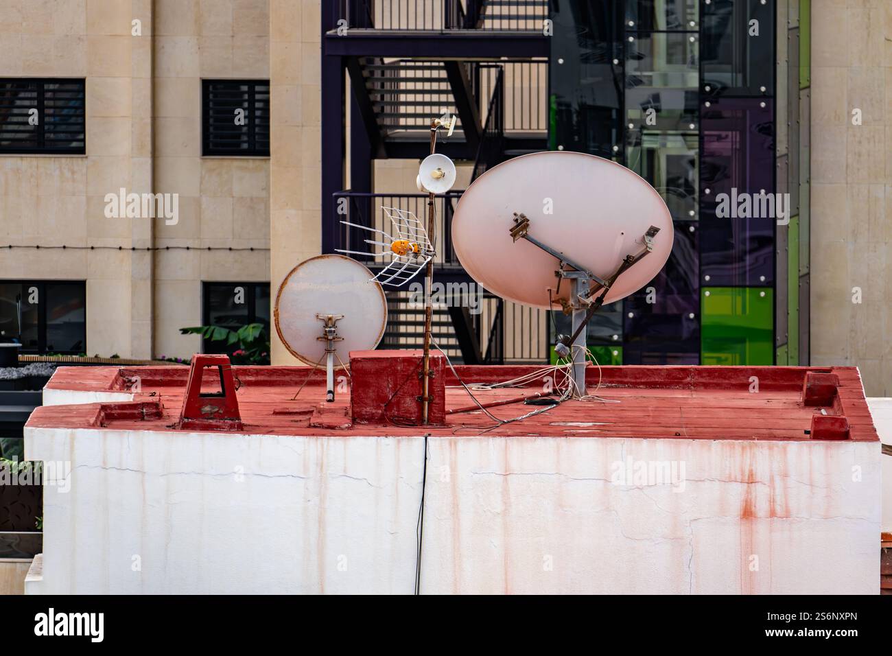 Two satellite dishes are on a roof of a building. The building is tall ...