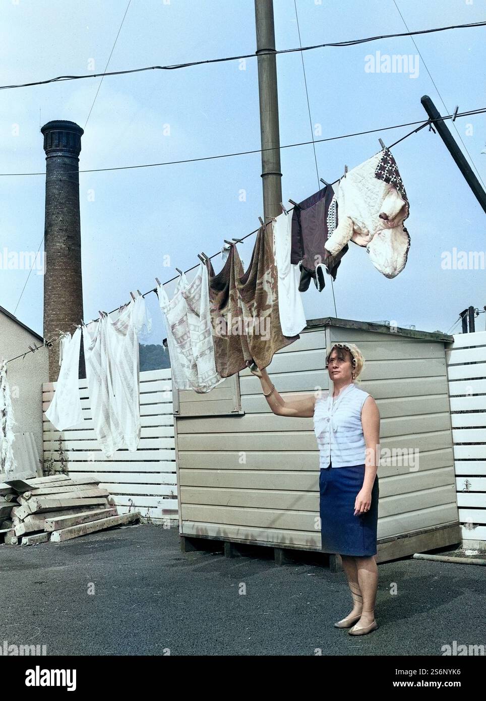 Woman hanging out her washing during the 1960s near factory chimneys ...