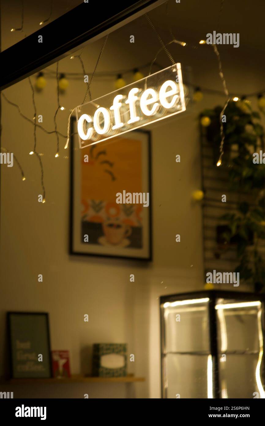 A nighttime coffee shop captured through its glass facade, where a warm ...