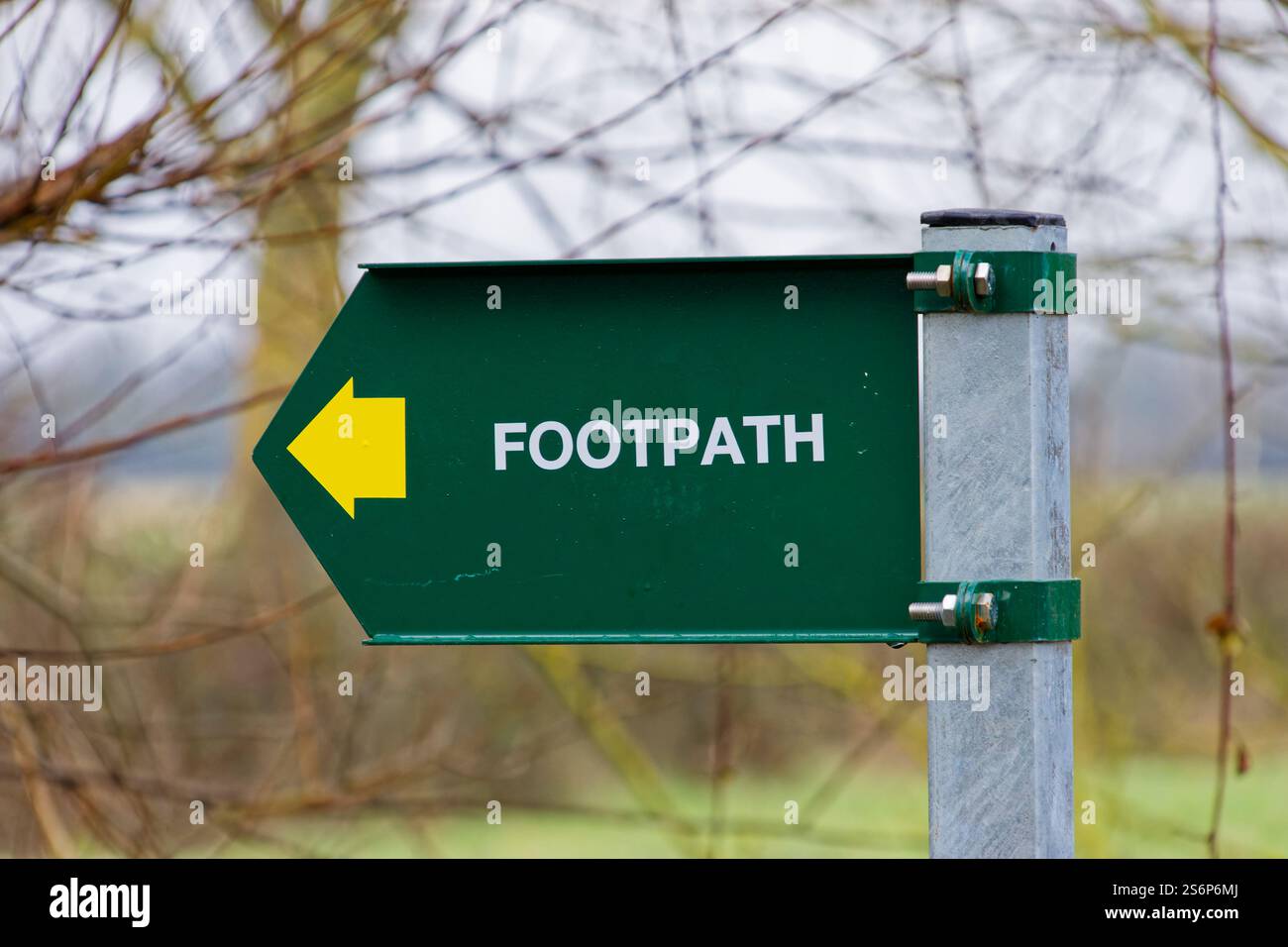 Green footpath sign with yellow arrow amidst a blurred background of ...