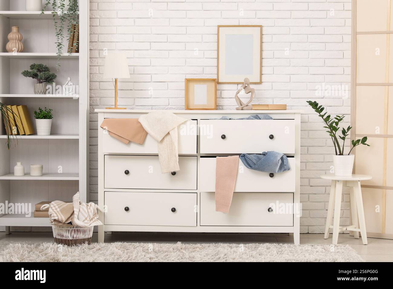 Interior of messy living room with shelving unit, scattered clothes and ...