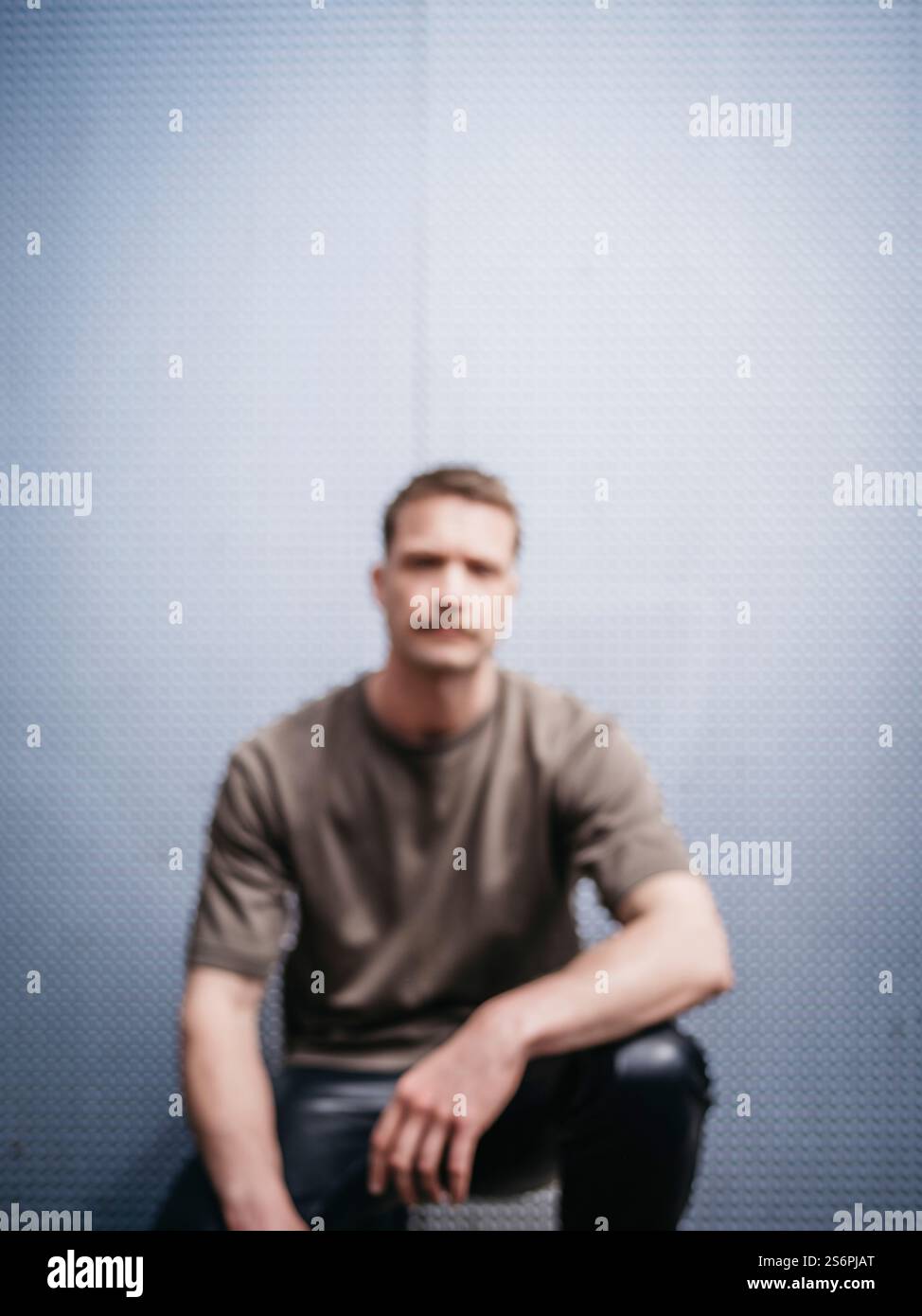 Man squatting in front of a light gray wall Stock Photo - Alamy