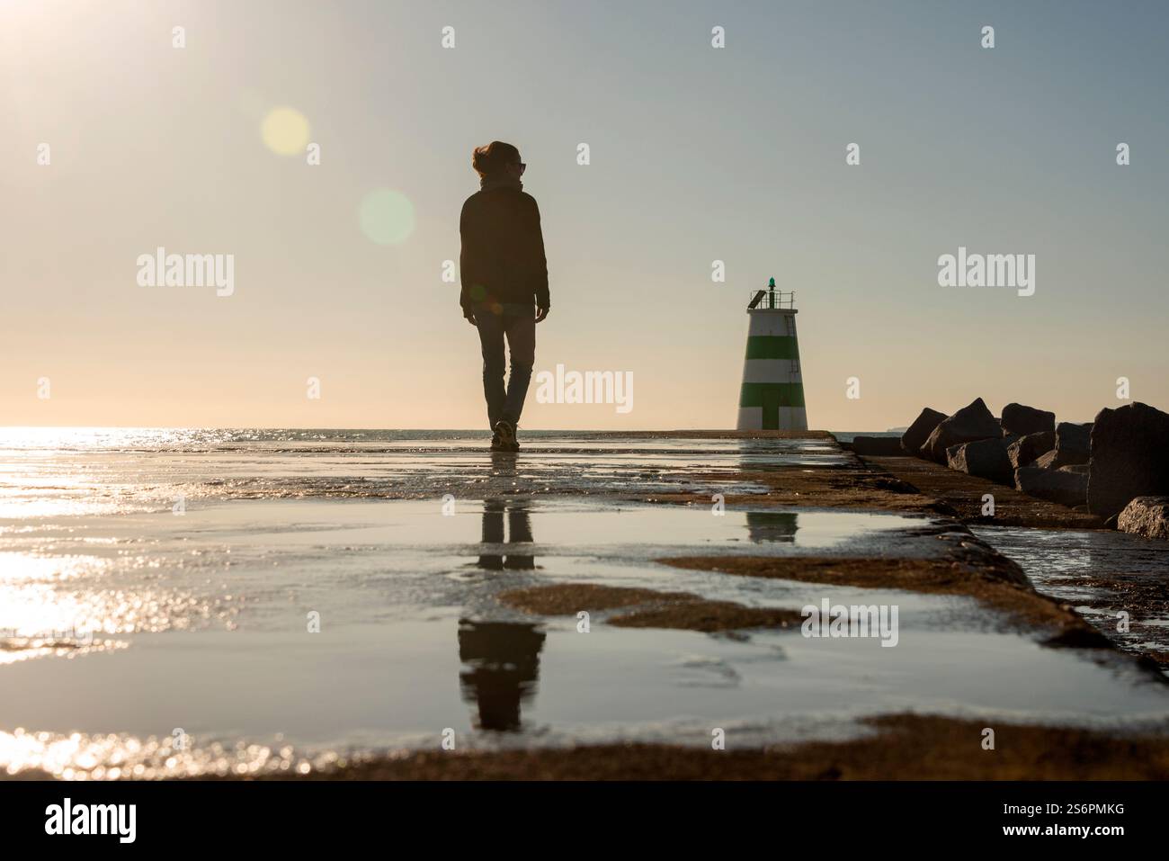silhouette of a woman walking along a causeway to a lighthouse with ...