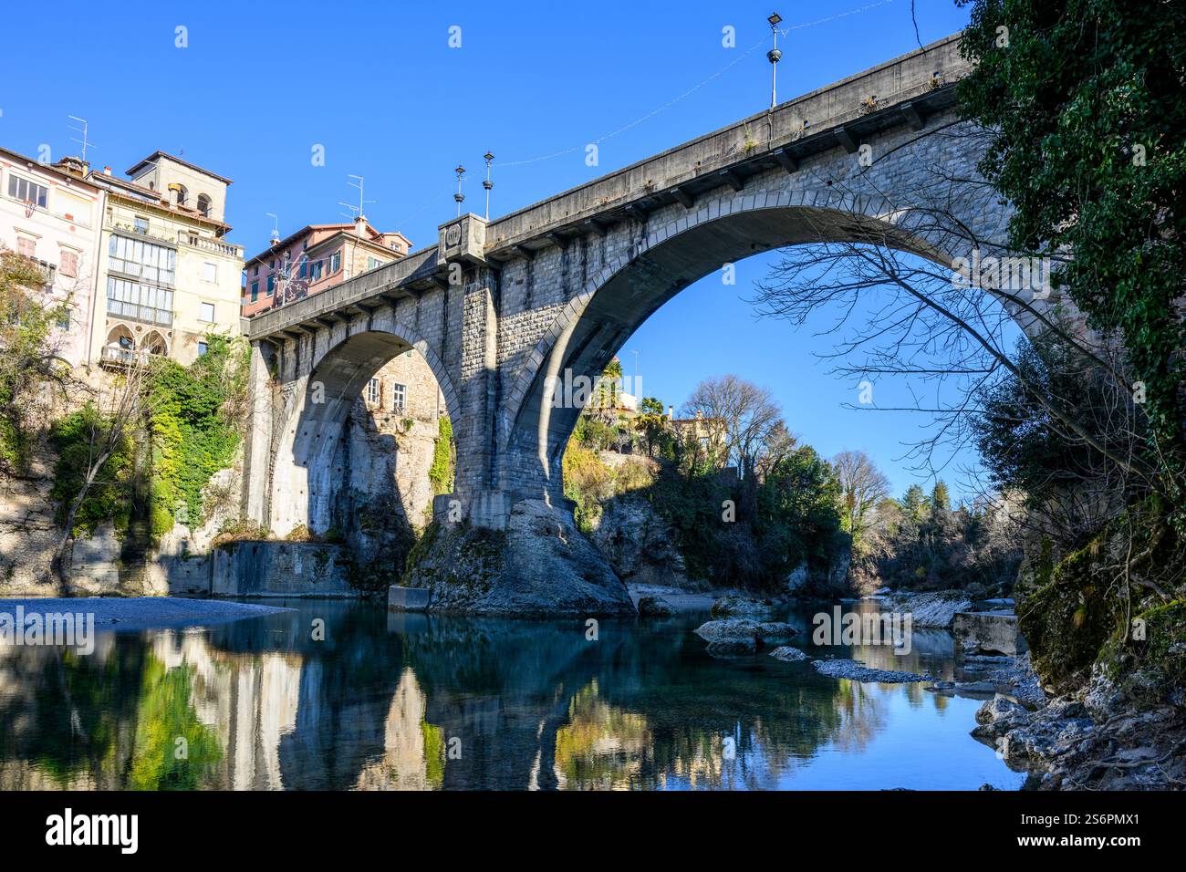 Stone arch bridge over a clear river, reflecting buildings and trees ...