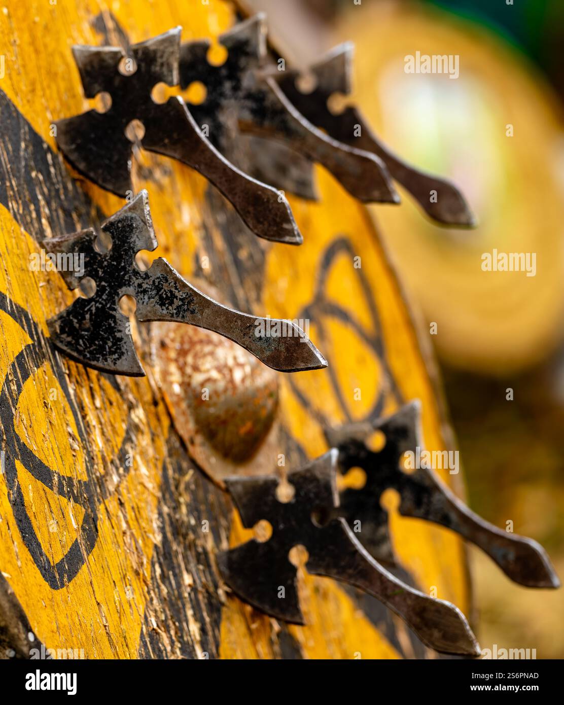 A group of black and silver axes are hanging on a yellow wooden board ...