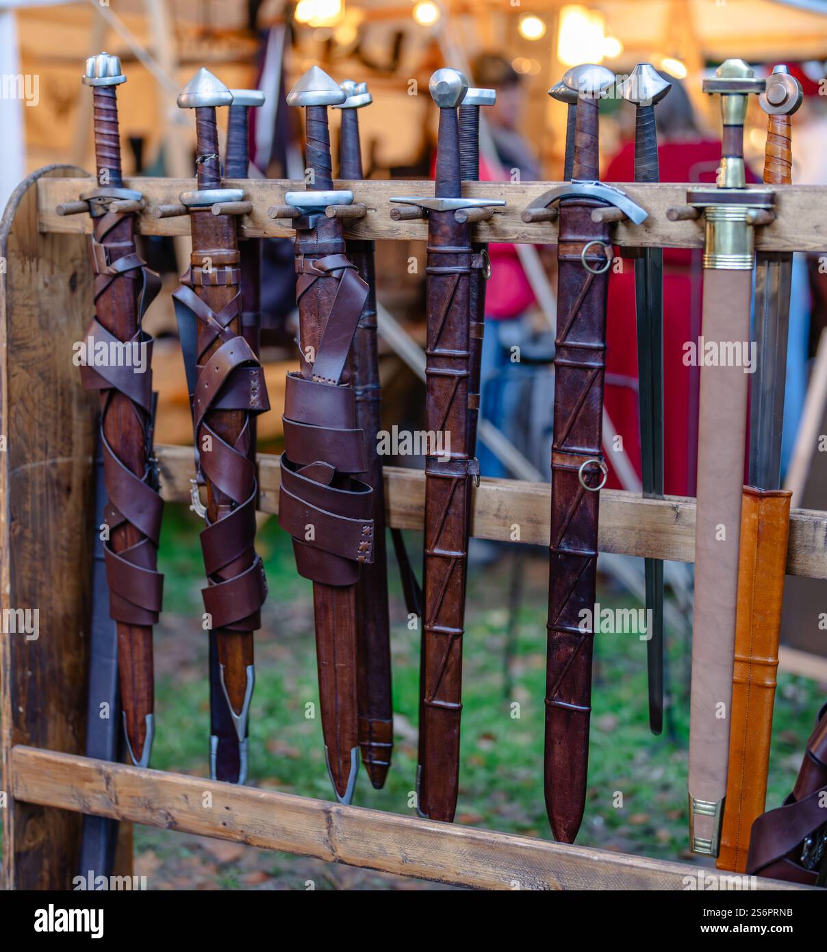 A row of swords are hanging on a wooden rack. The swords are of ...