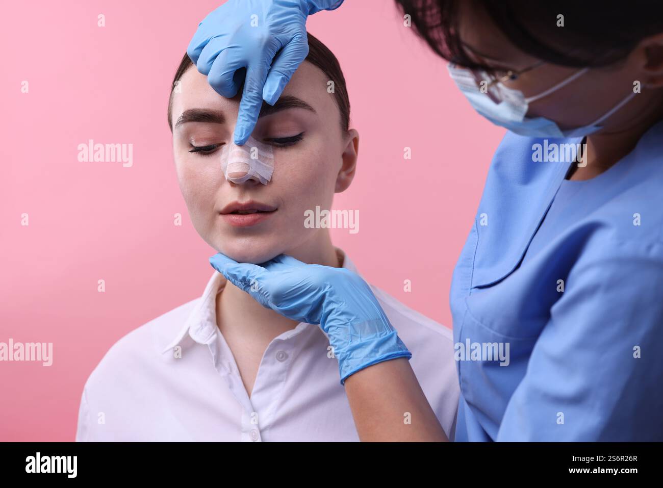 Doctor checking patient's nose after plastic surgery operation on pink ...