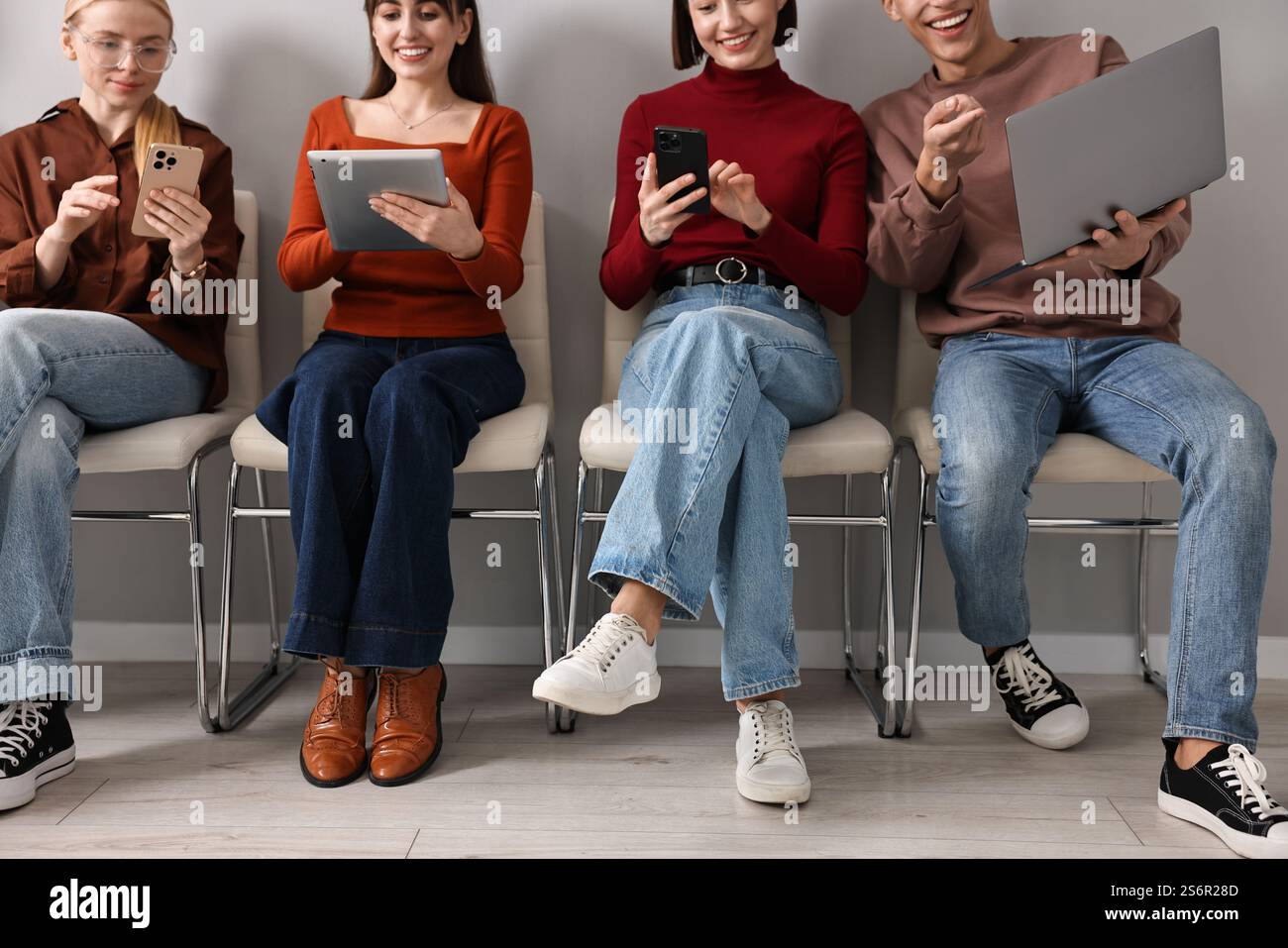 Group of people using different gadgets on chairs near grey wall ...