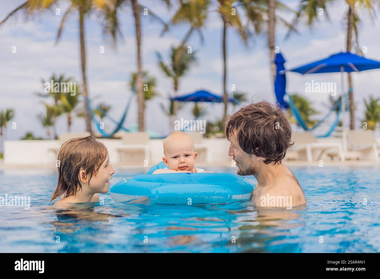 A father enjoys swimming in a pool with his son and infant, who is ...