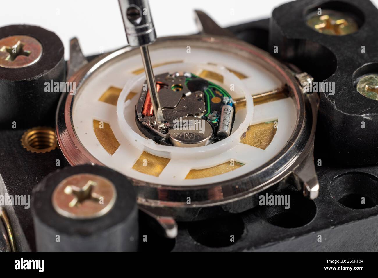 Watchmaker loosening the battery retaining clip with a watchmaker's screwdriver, detail, white ...