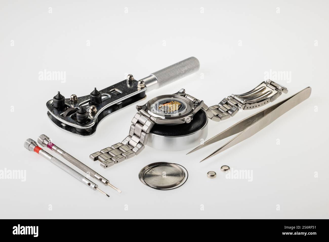 Watch case open, lying on watch case cushion, watch battery, watchmaker's tool, white background ...