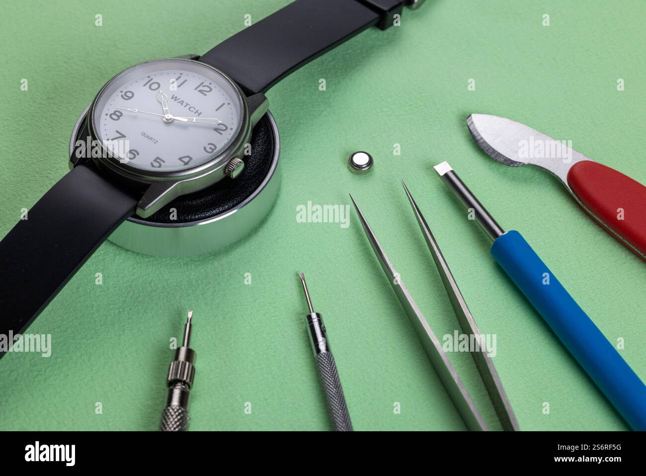 Wristwatch lying on watch cushion, watchmaker's tool, green background, symbol photo, battery ...