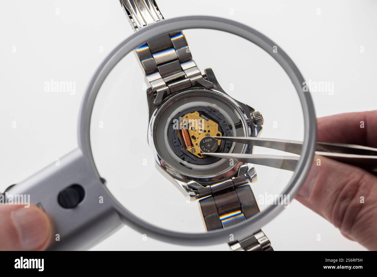 Magnifying glass, view of open watch case, tweezers, watch battery ...