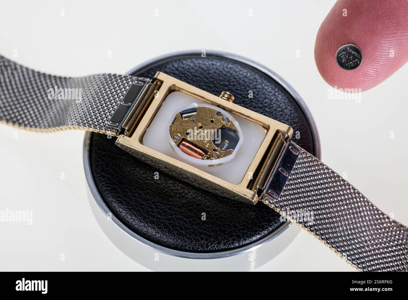 Watch case open, watch battery lying on fingertip, detail, white ...