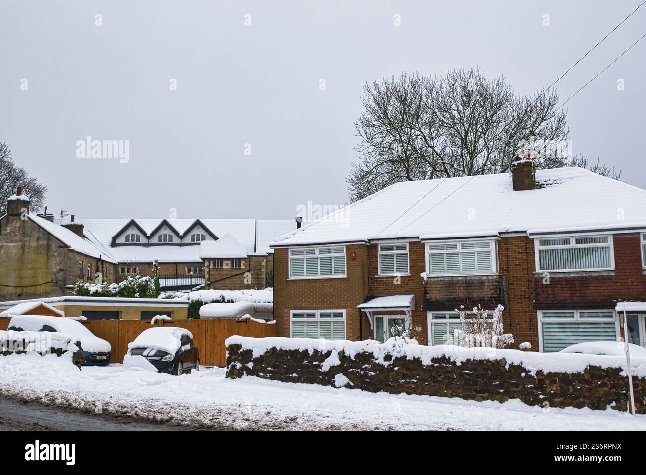 Snow-covered residential homes and cars. A two-story brick house with ...
