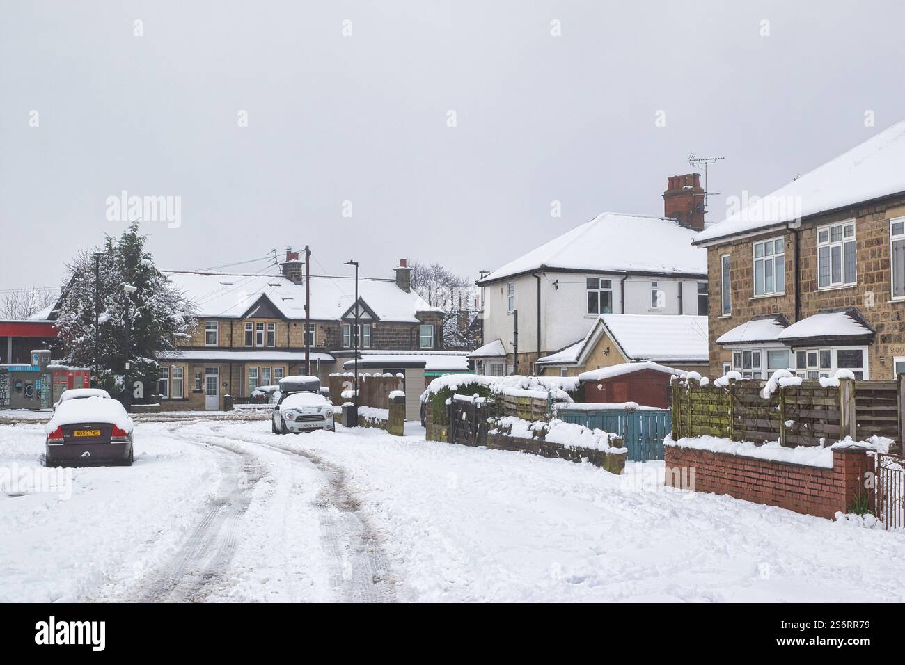 Snow-covered residential street scene with parked cars in front of two ...