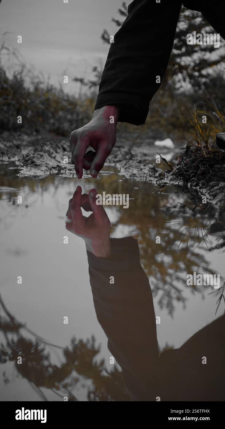 A hand reaching towards a puddle, creating a reflection on the water's ...