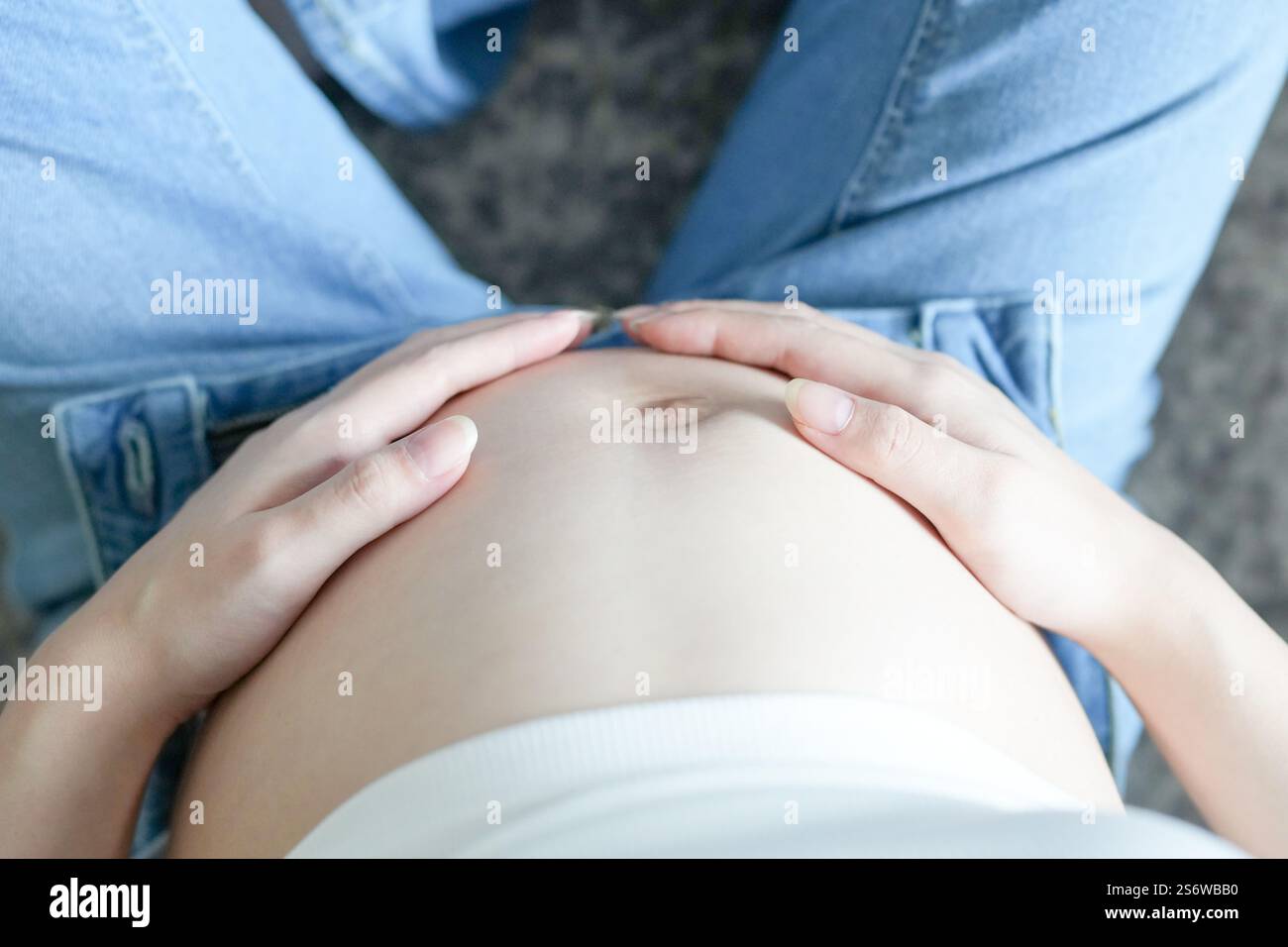 A Japanese pregnant woman in her 20s, wearing a dress that shows her stomach, sits on a sofa in ...