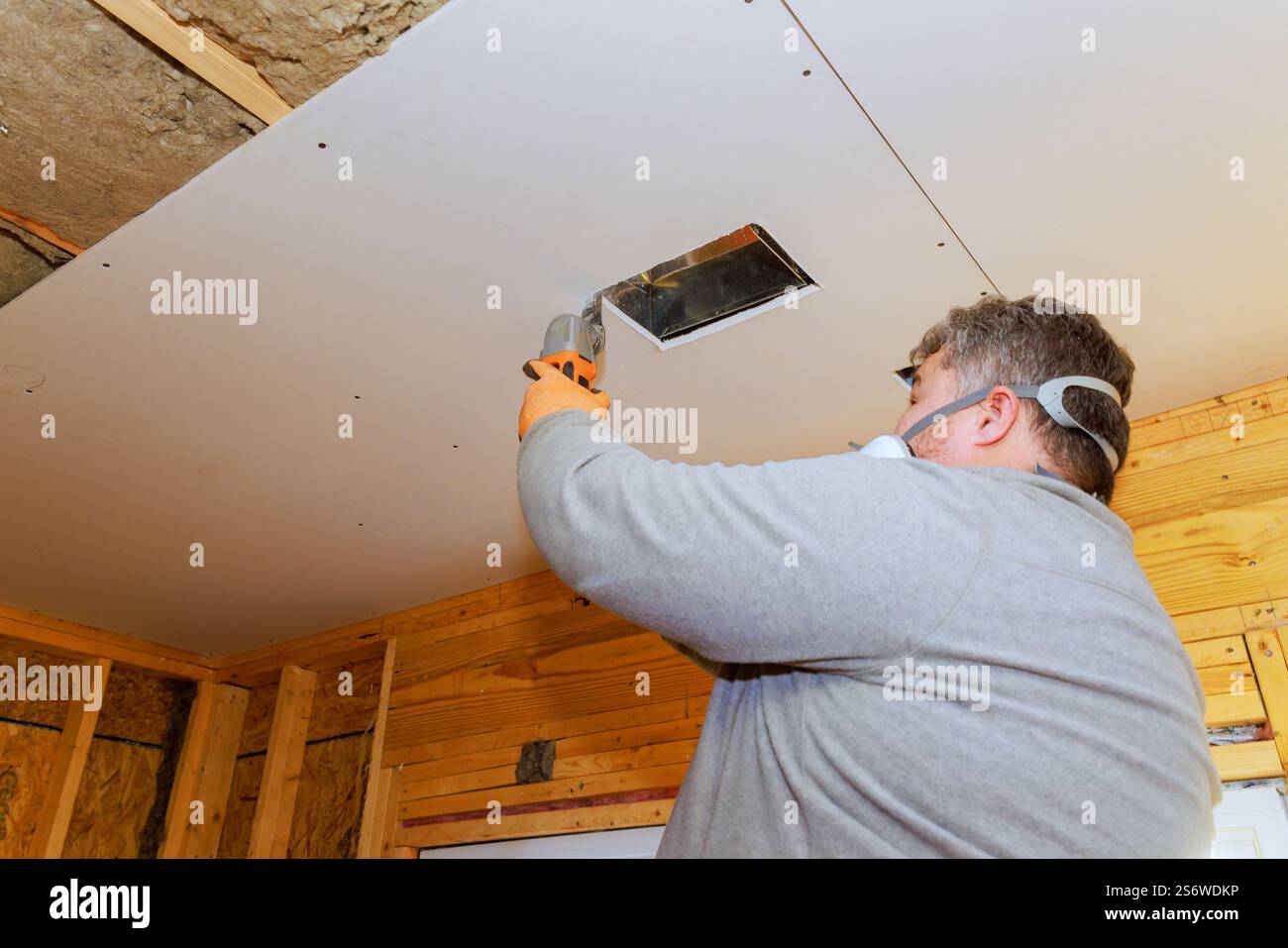 Worker carefully fits ventilation into ceiling of home during ...