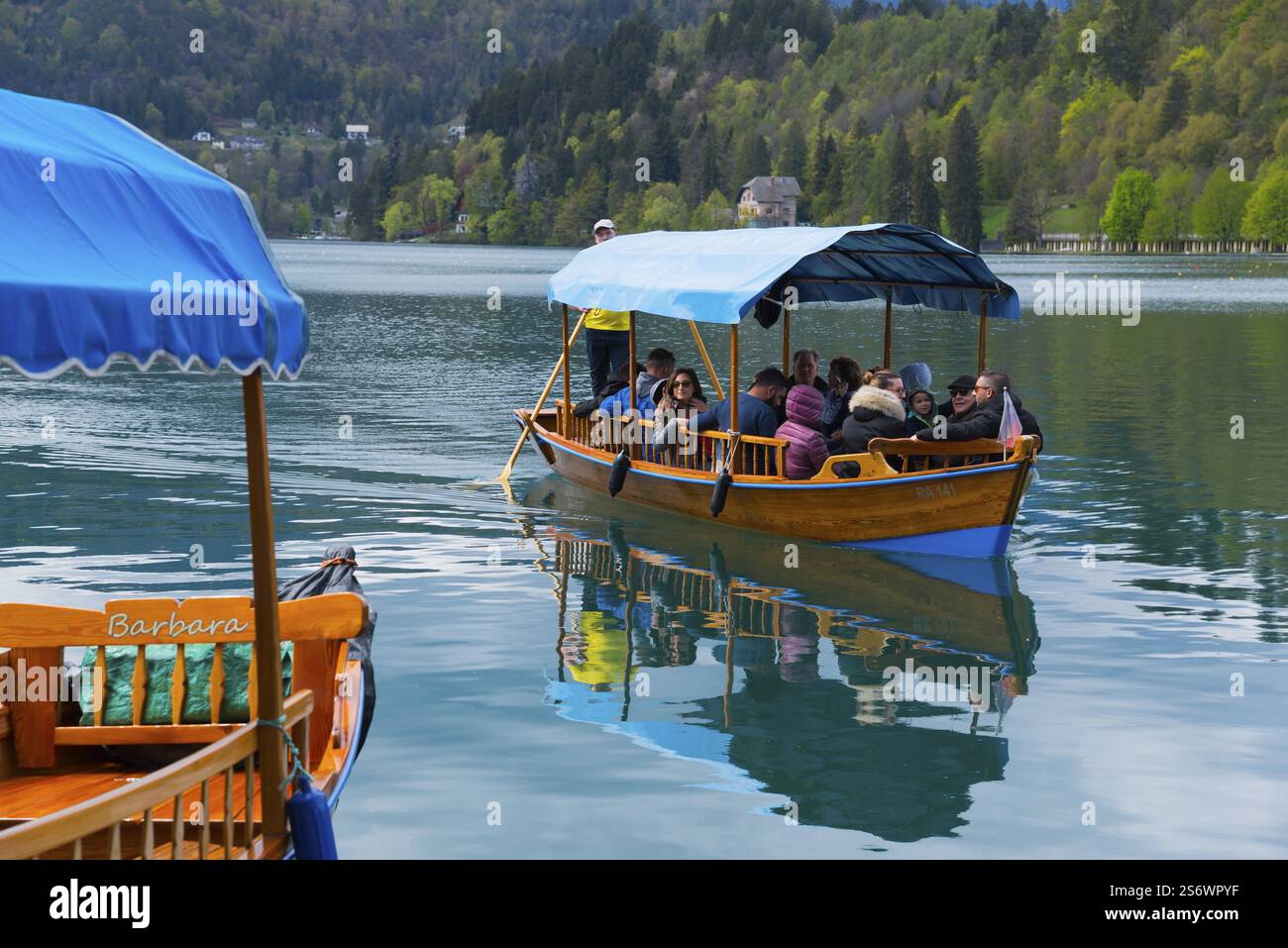 A wooden boat full of people sails on a calm lake surrounded by ...