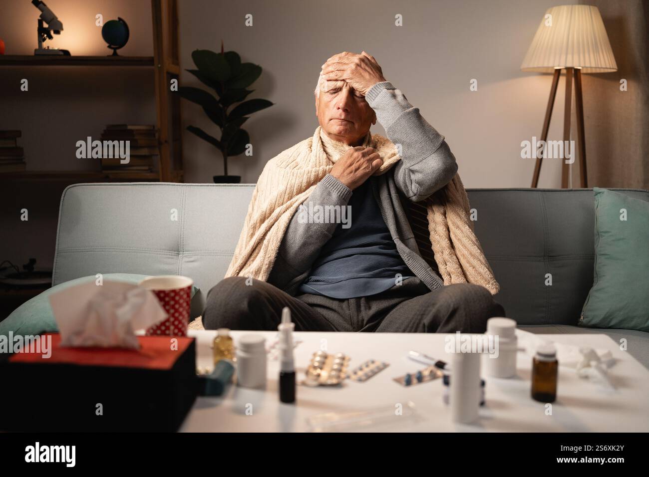 Elderly man suffering from flu and fever sits wrapped in blanket on ...