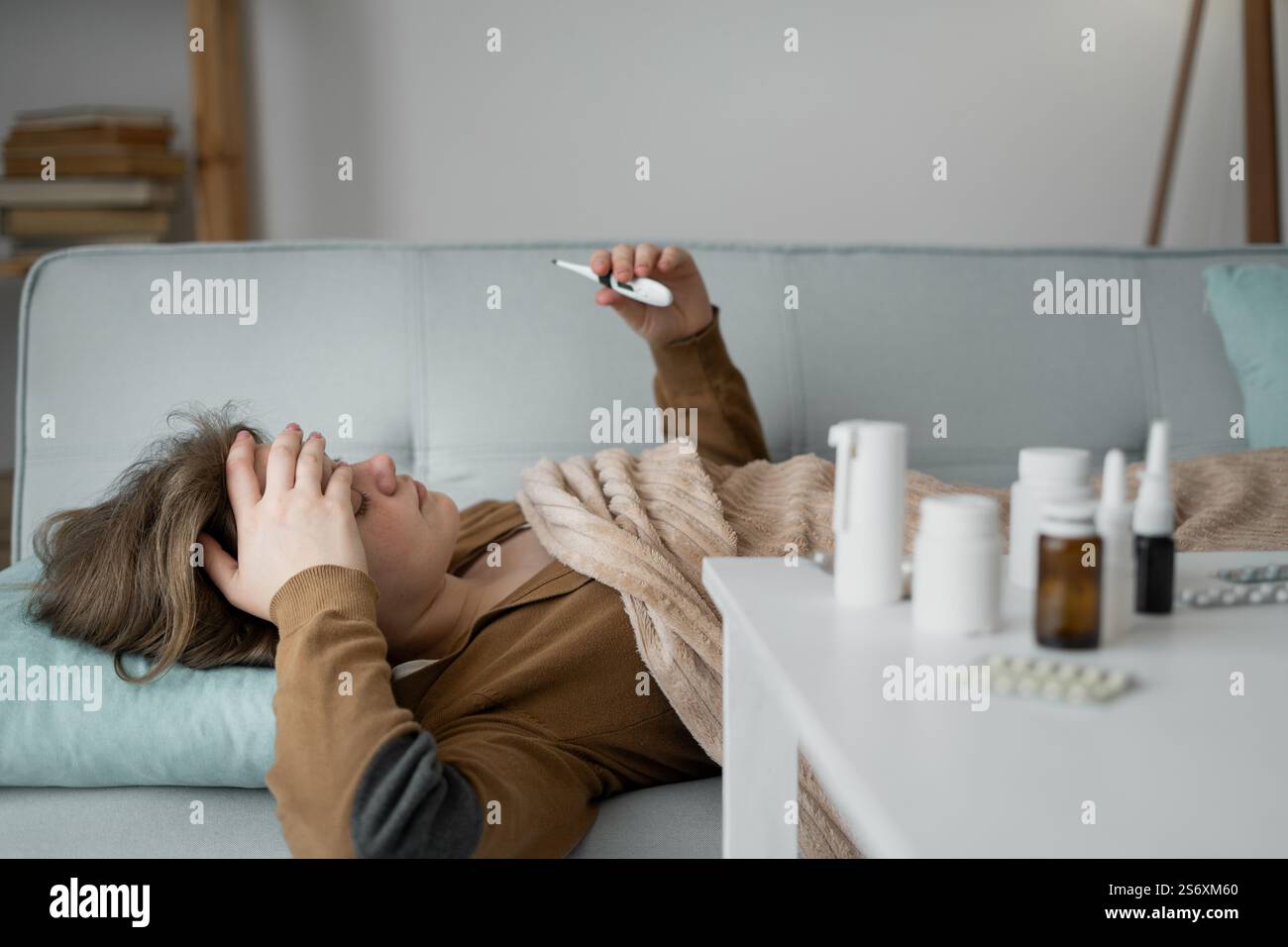 sick woman lying on sofa holding thermometer and touching forehead with ...