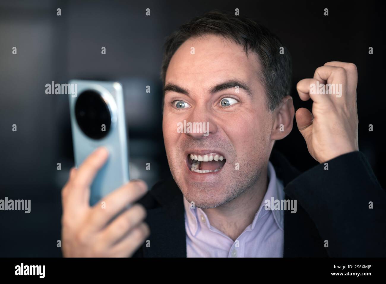 A man in a pink shirt and stares at his smartphone with a look of shock ...