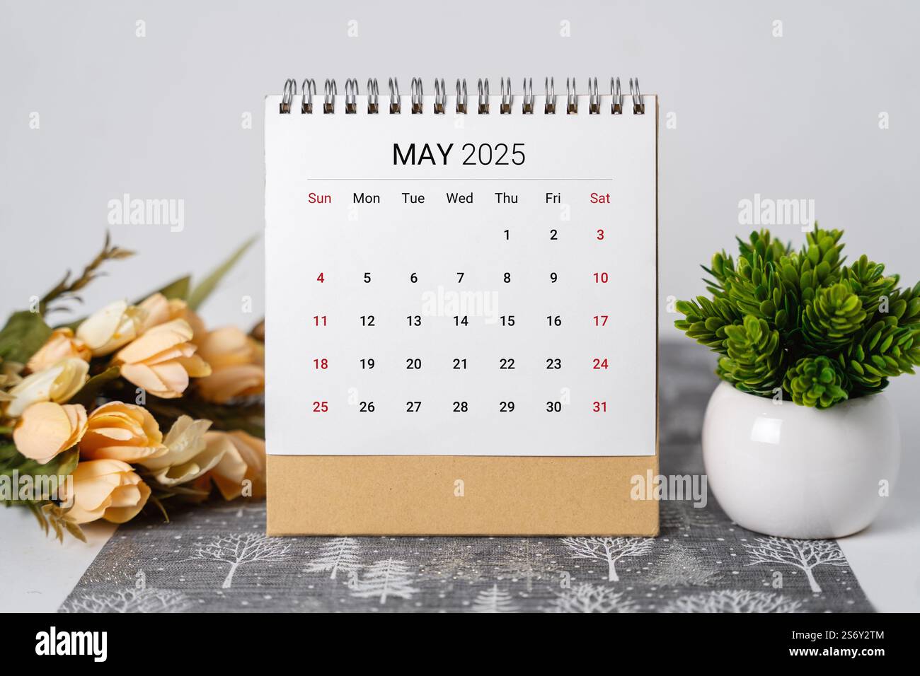 A desk calendar showing May 2025, placed on a table with a flower ...