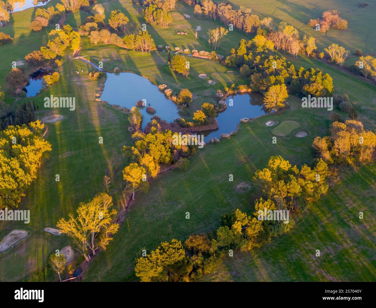 Aerial view of a golf course with ponds and trees bathed in golden ...