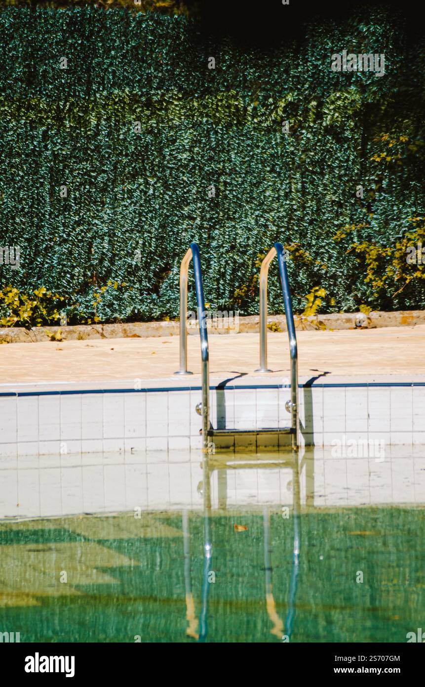 ladder of dirty swimming pool with draining water before cleaning for ...